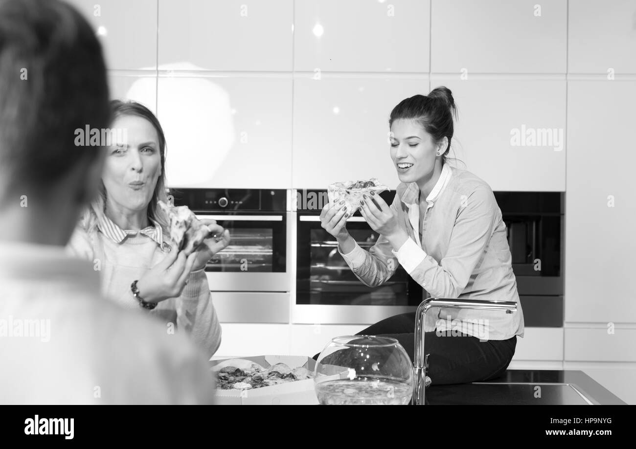 family and friends preparing lunch and eating pizza together at home in ...