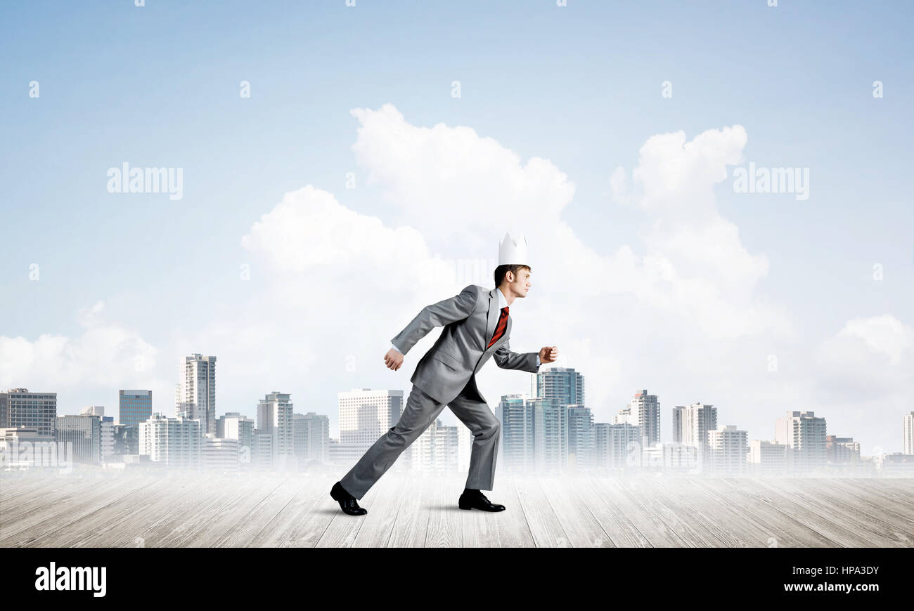 Young handsome businessman wearing white paper crown running in a hurry ...