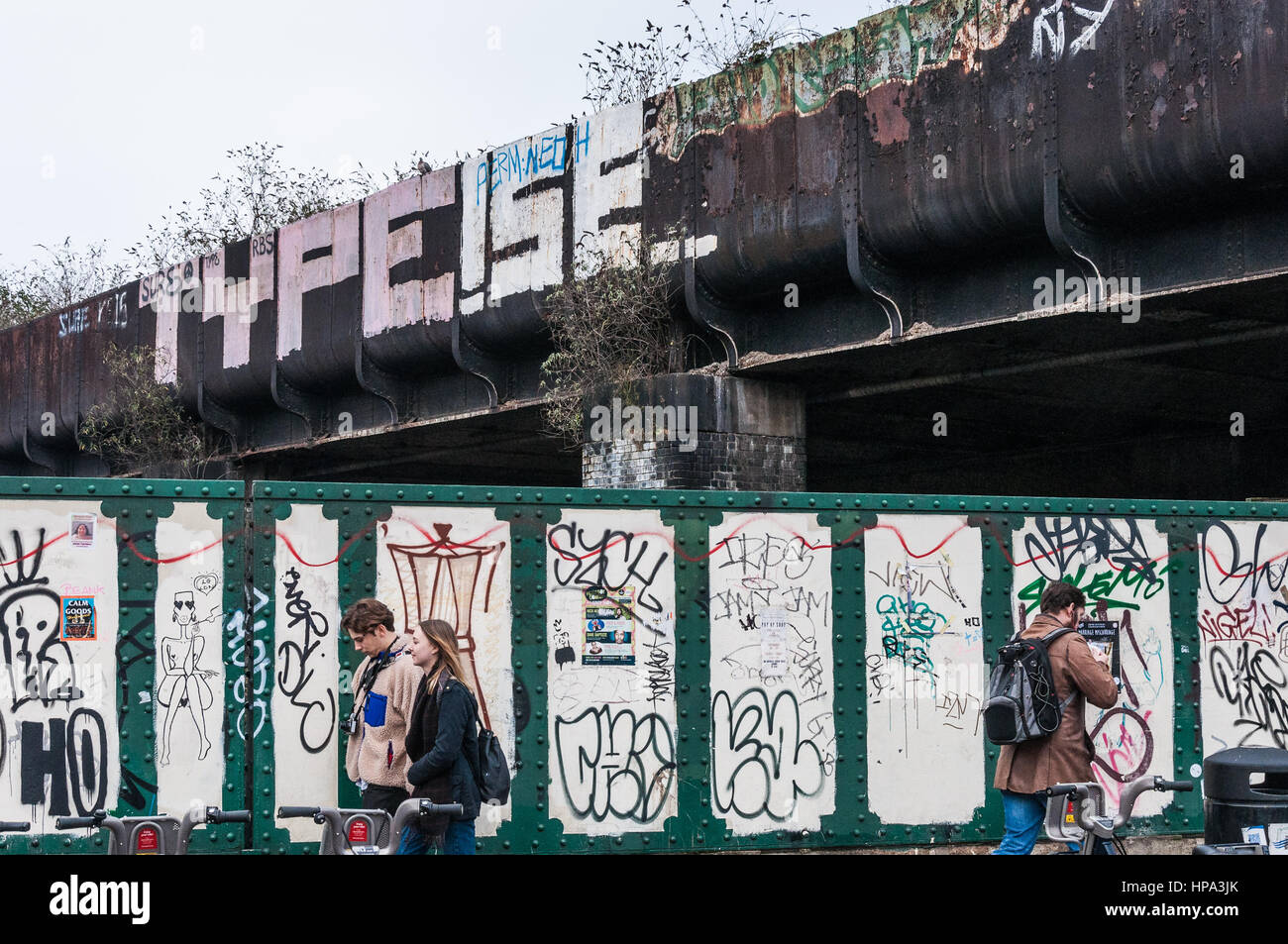 A scruffy, overgrown, graffiti adorned railway viaduct crossing Brick ...
