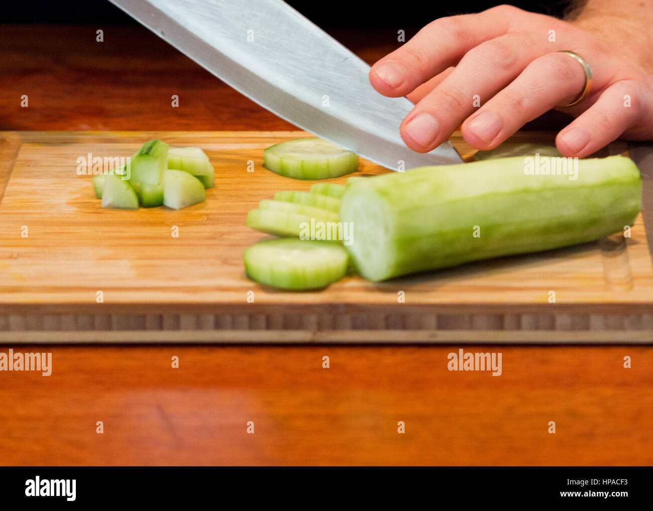 A male hand slicing a cucumber on a wooden cutting board Stock Photo ...