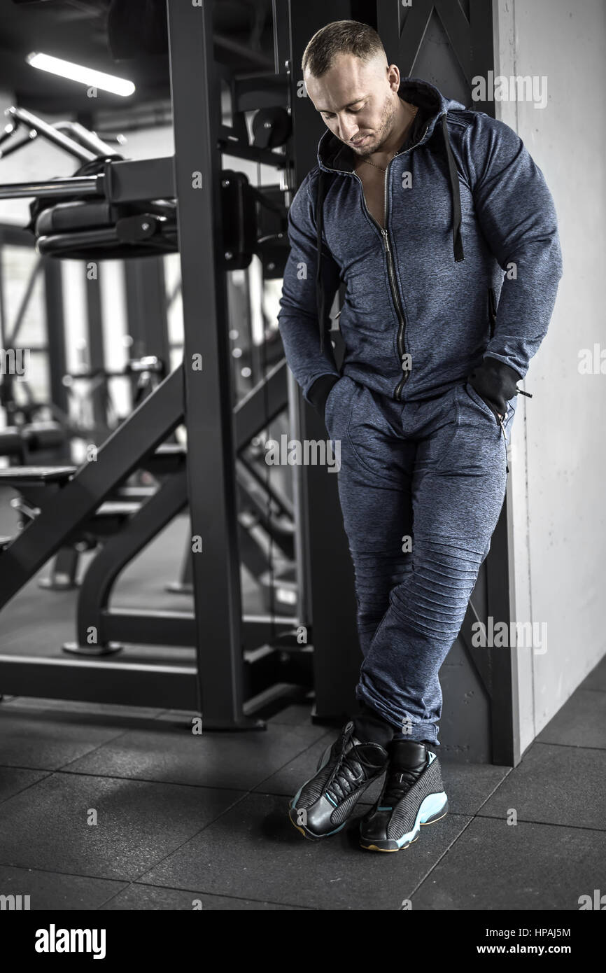 Strong man with big muscles leans on the wall in the gym. He looks ...