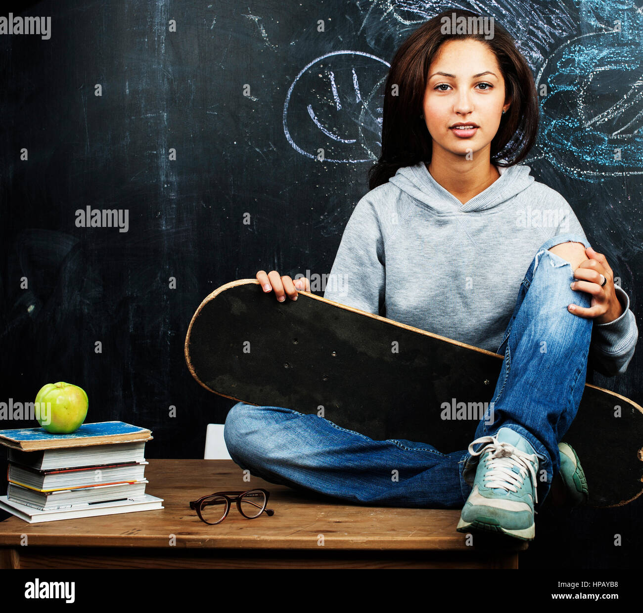 young cute teenage girl in classroom at blackboard seating on table ...