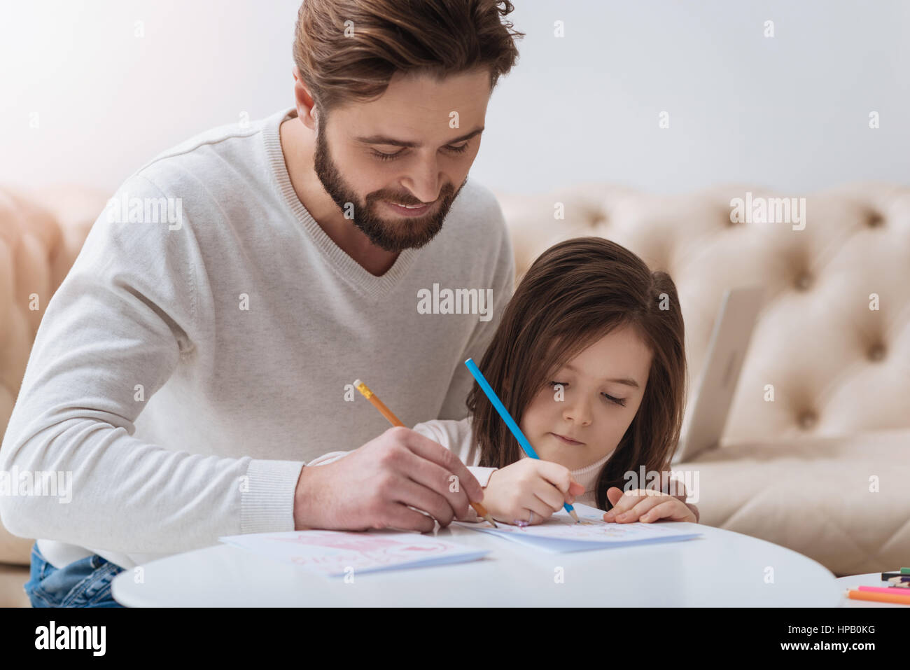 Drawing a picture. Pleasant positive caring father sitting next to his ...