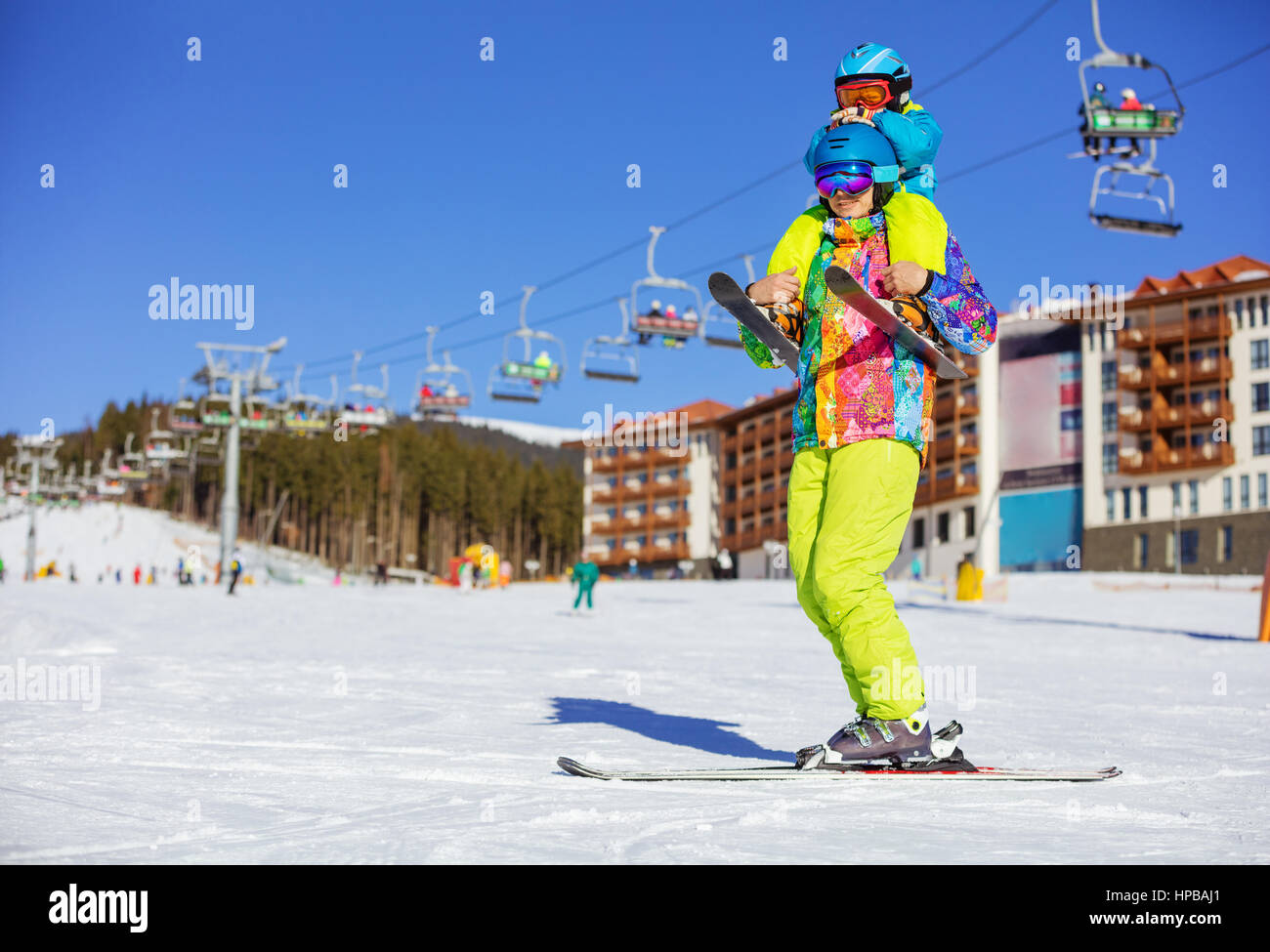 Father carrying tired son in skiing outfit on shoulders. Standing on ...