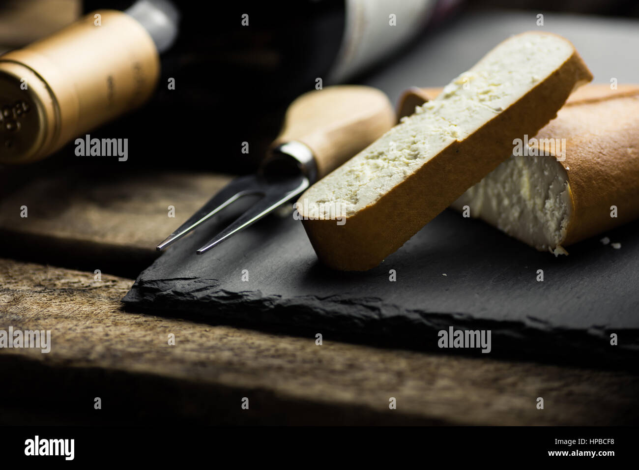Chunk and thick cut off slice of smoked goat cheese with fork on black ...