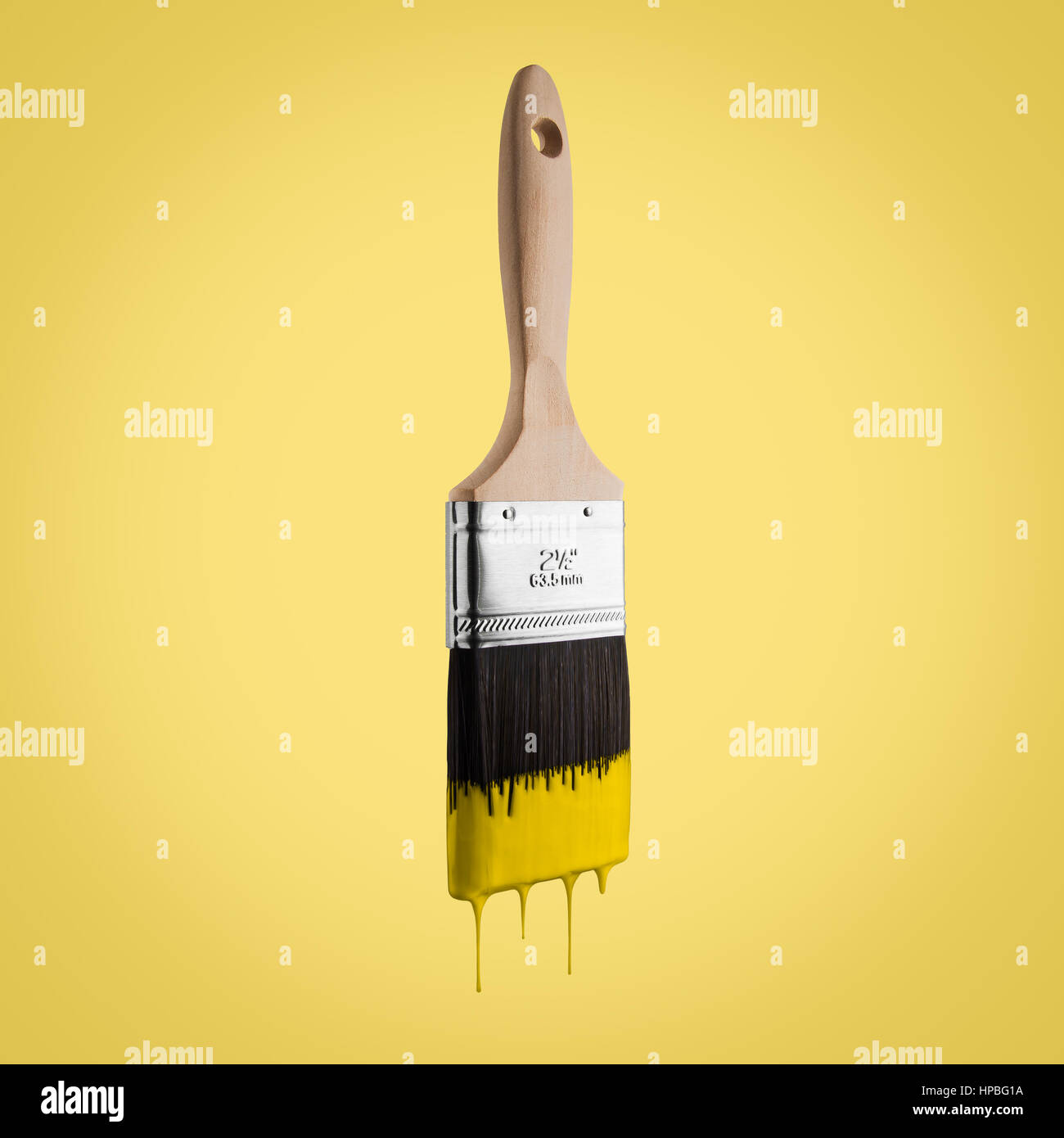 Paintbrush loaded with yellow color dripping off the bristles, on ...
