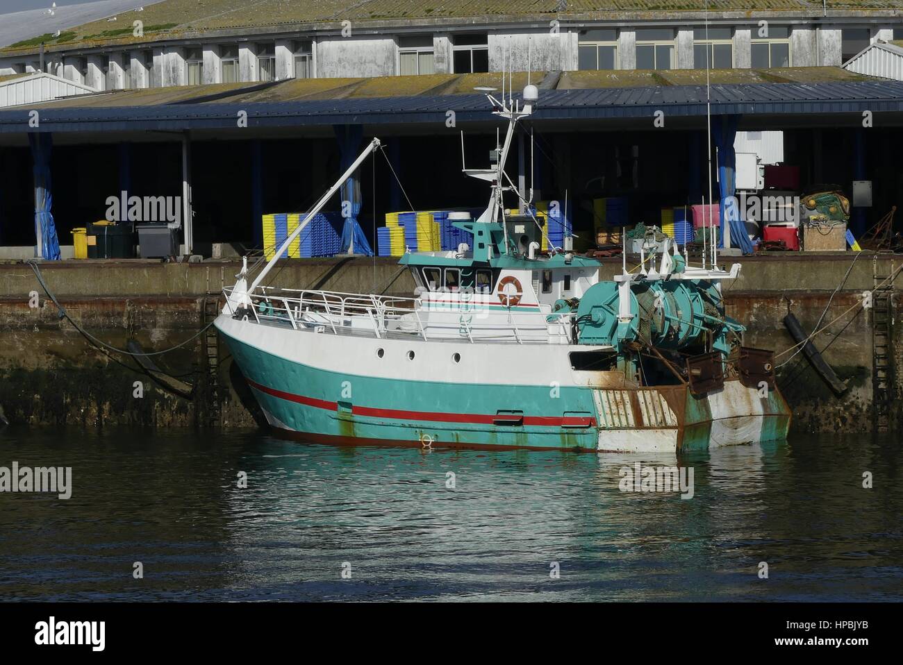 Turquoise fishing boat alongside the dock with warehouse in the ...
