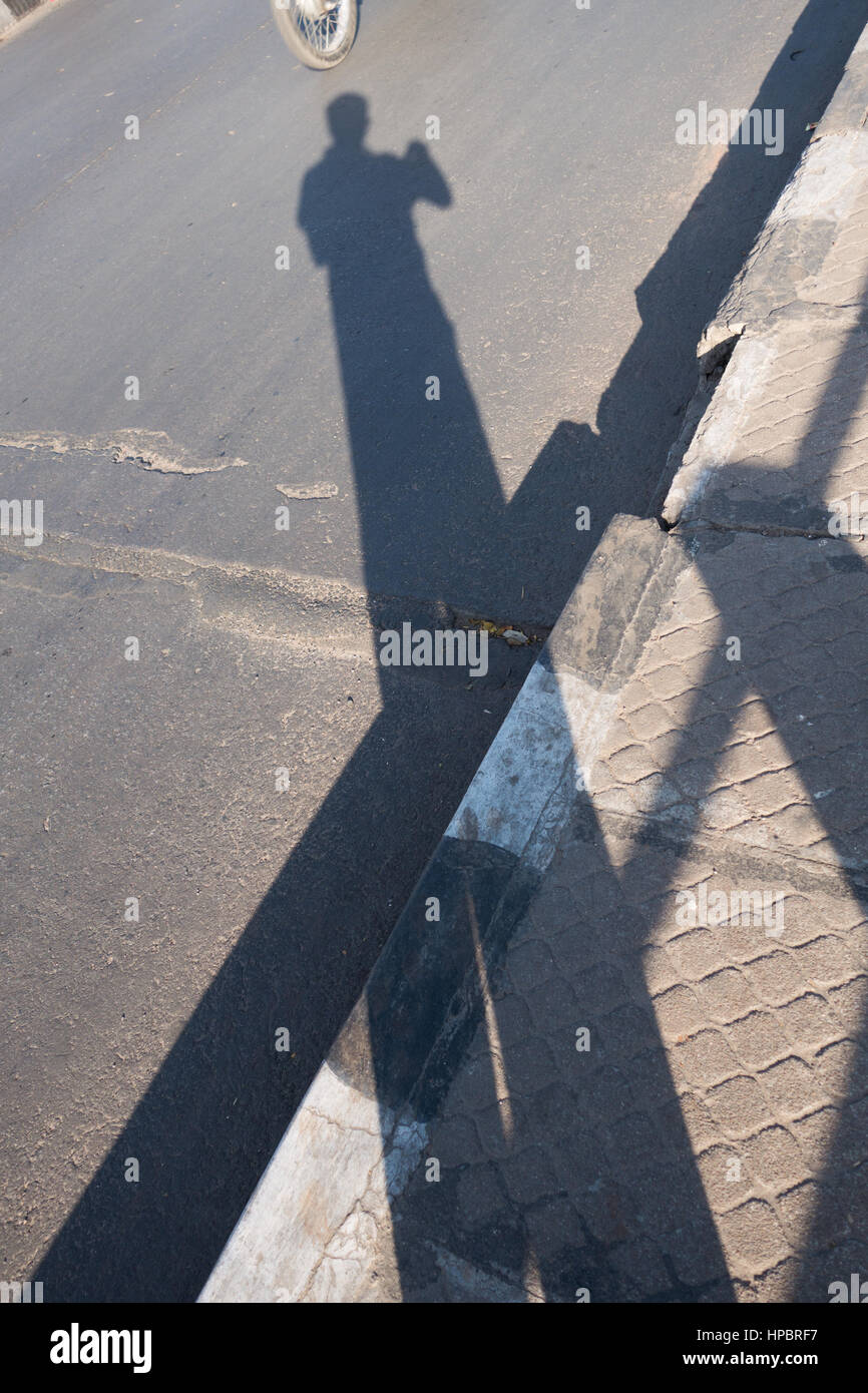 Indian man taking a picture of his own shadow standing on a sidewalk ...