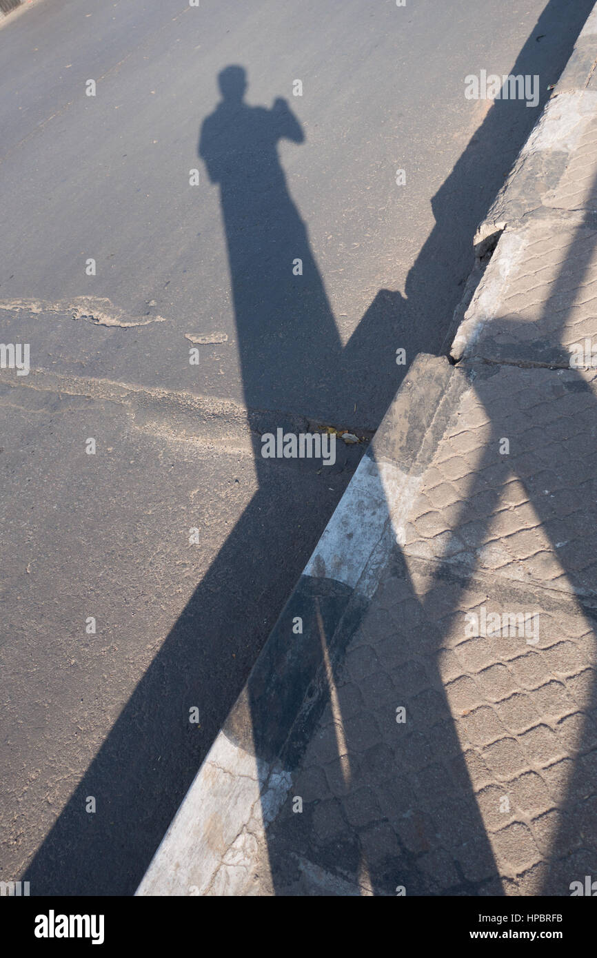 Indian man taking a picture of his own shadow standing on a sidewalk ...
