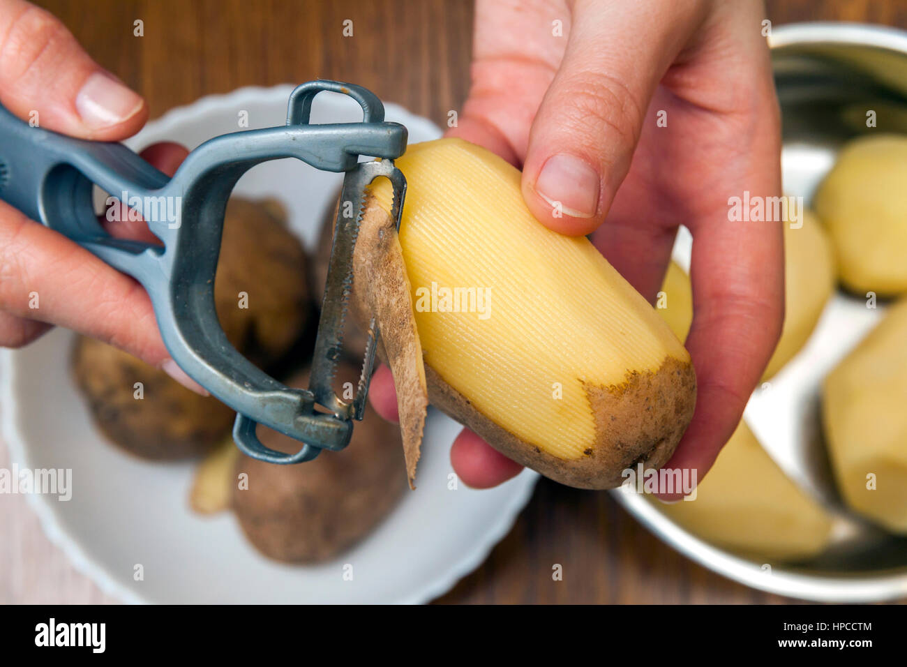 Detail of woman hands peeling fresh yellow potato with kitchen peeler ...