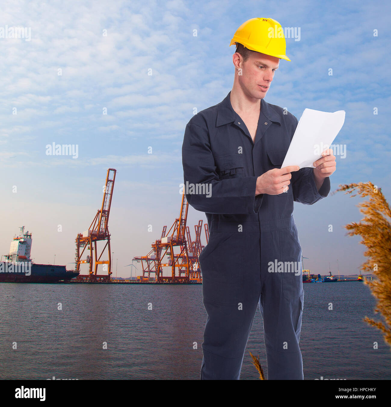 Young worker at harbor with cranes on background Stock Photo - Alamy