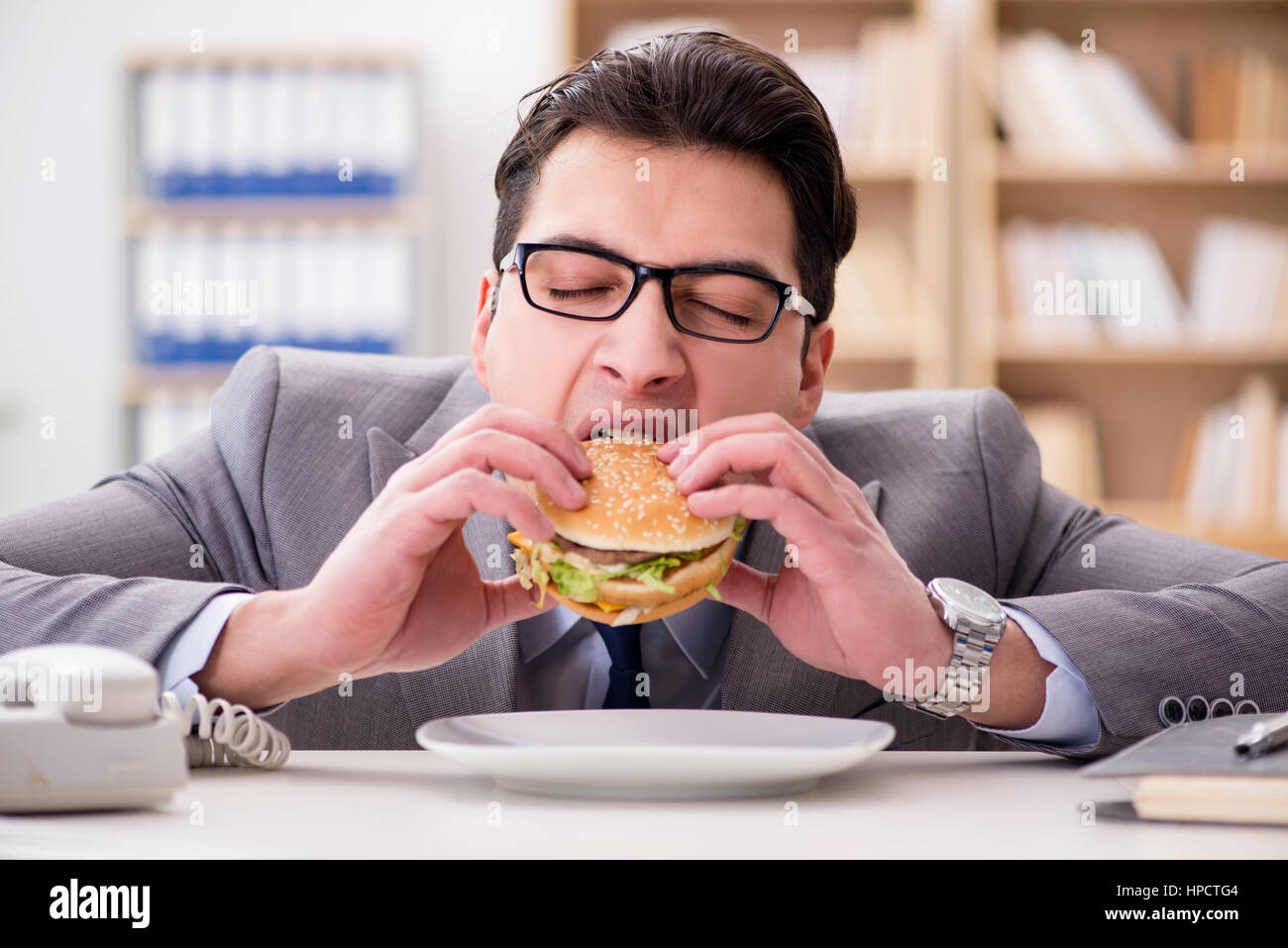 Hungry funny businessman eating junk food sandwich Stock Photo - Alamy
