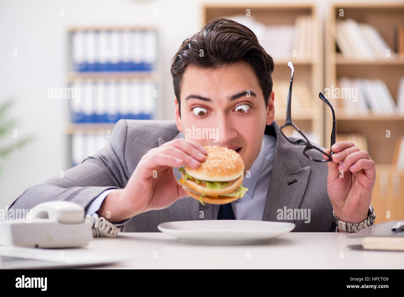 Hungry funny businessman eating junk food sandwich Stock Photo - Alamy