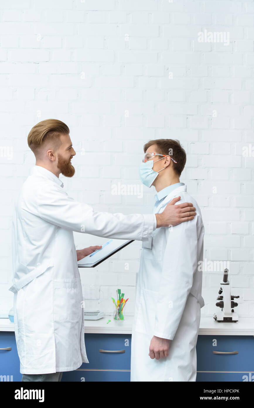 side view of scientists in white coats discussing experiment results in ...