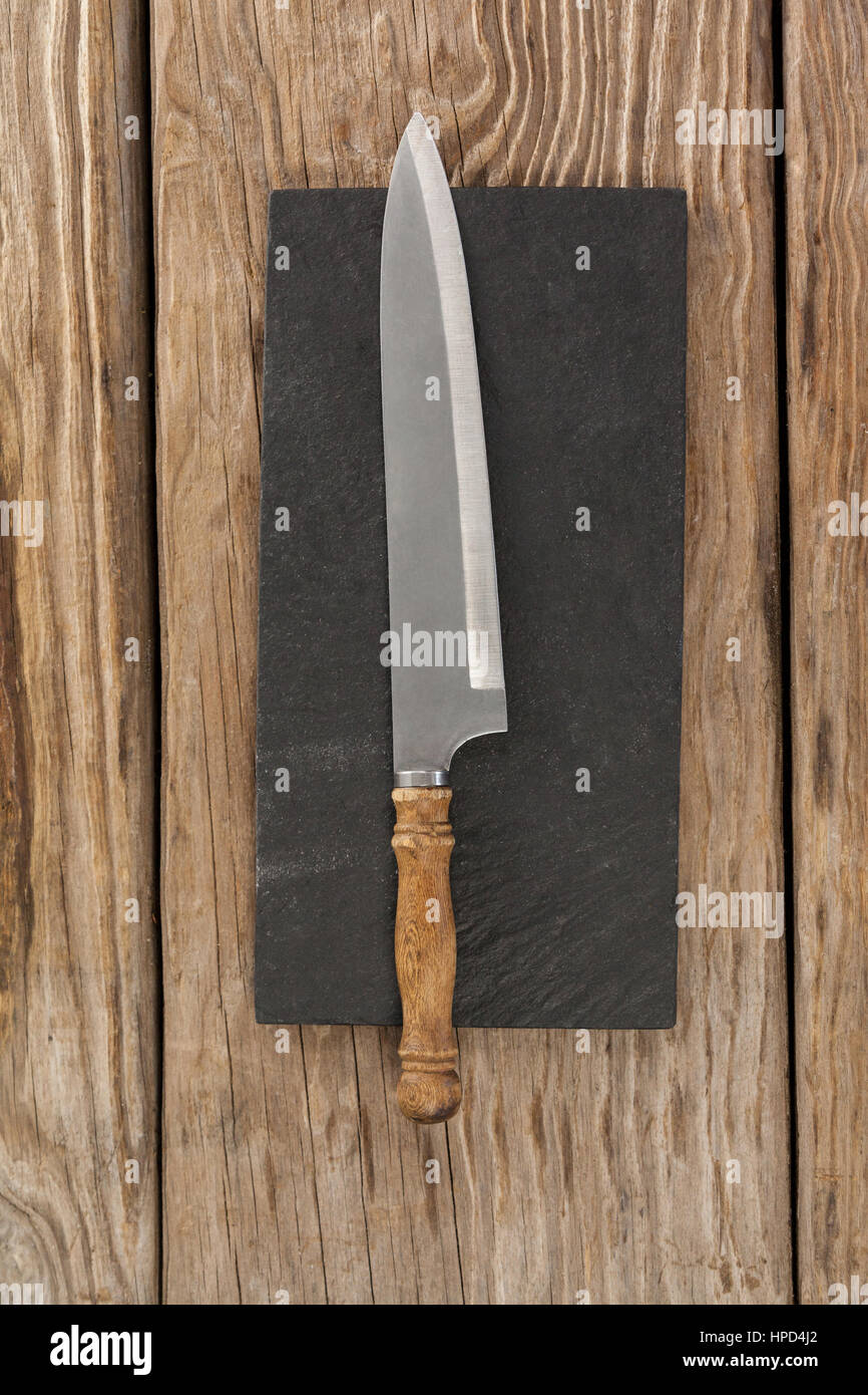 Knife on black slate plate against wooden background Stock Photo - Alamy