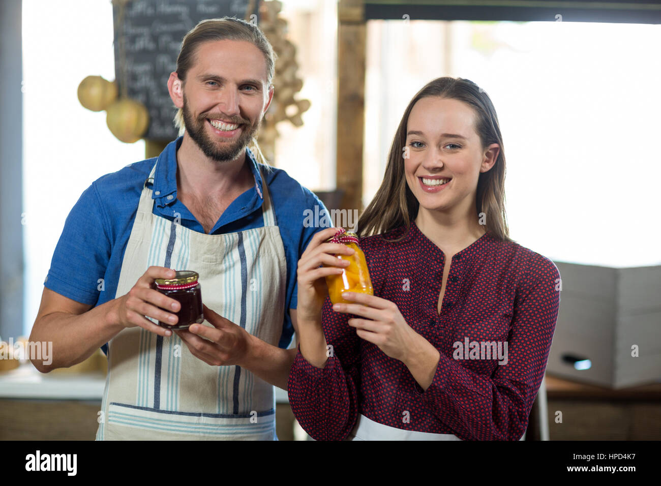 Portrait of shop assistants interacting while holding jam and pickle ...