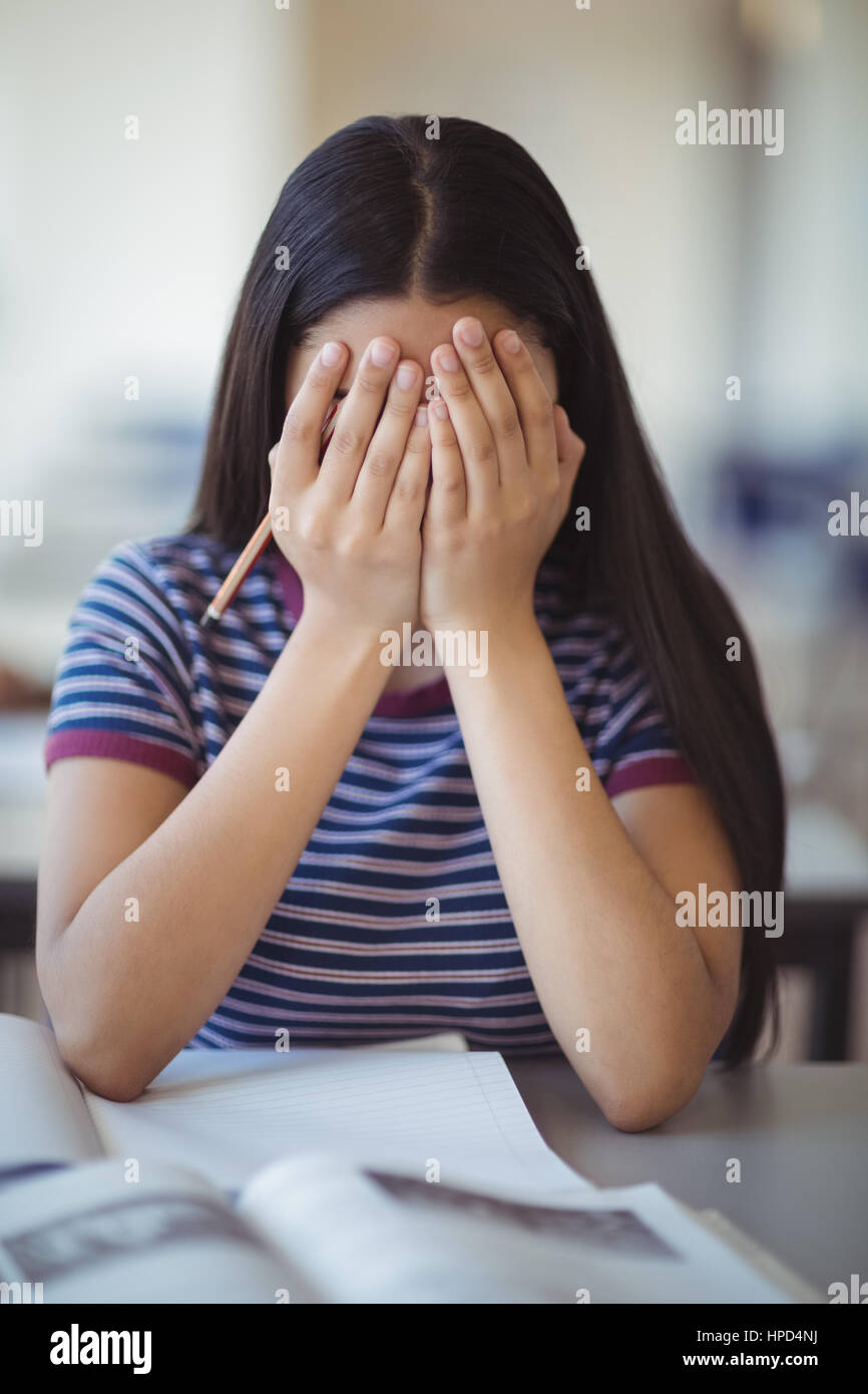 Stressed schoolgirl doing covering her face in classroom at school ...
