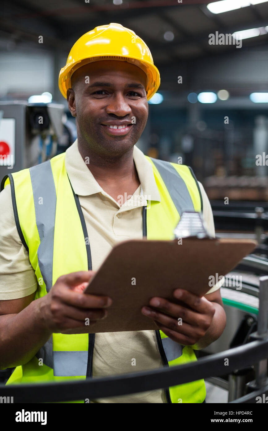 Portrait of smiling factory worker holding clipboard in factory Stock ...
