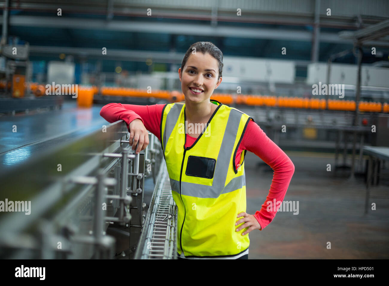Portrait of smiling female factory worker standing next to production ...