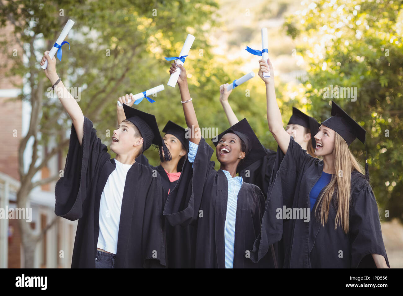 Smiling graduate school kids standing with degree scroll in campus at ...