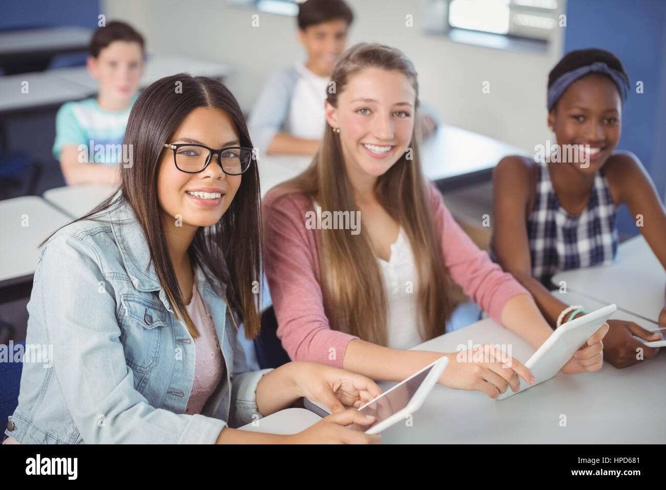 Portrait of students holding digital tablet in classroom at school ...