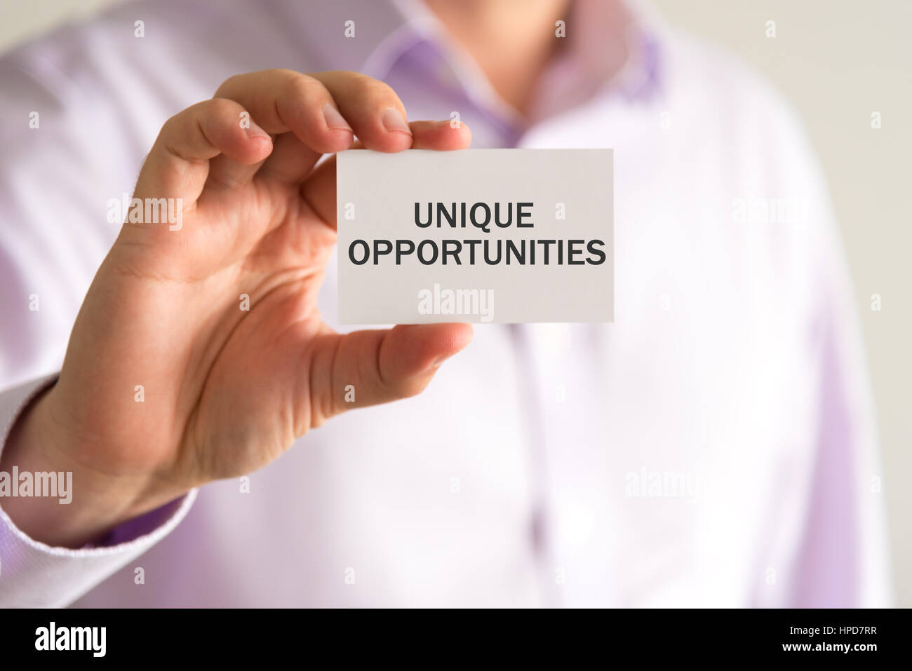 Closeup on businessman holding a card with text UNIQUE OPPORTUNITIES ...
