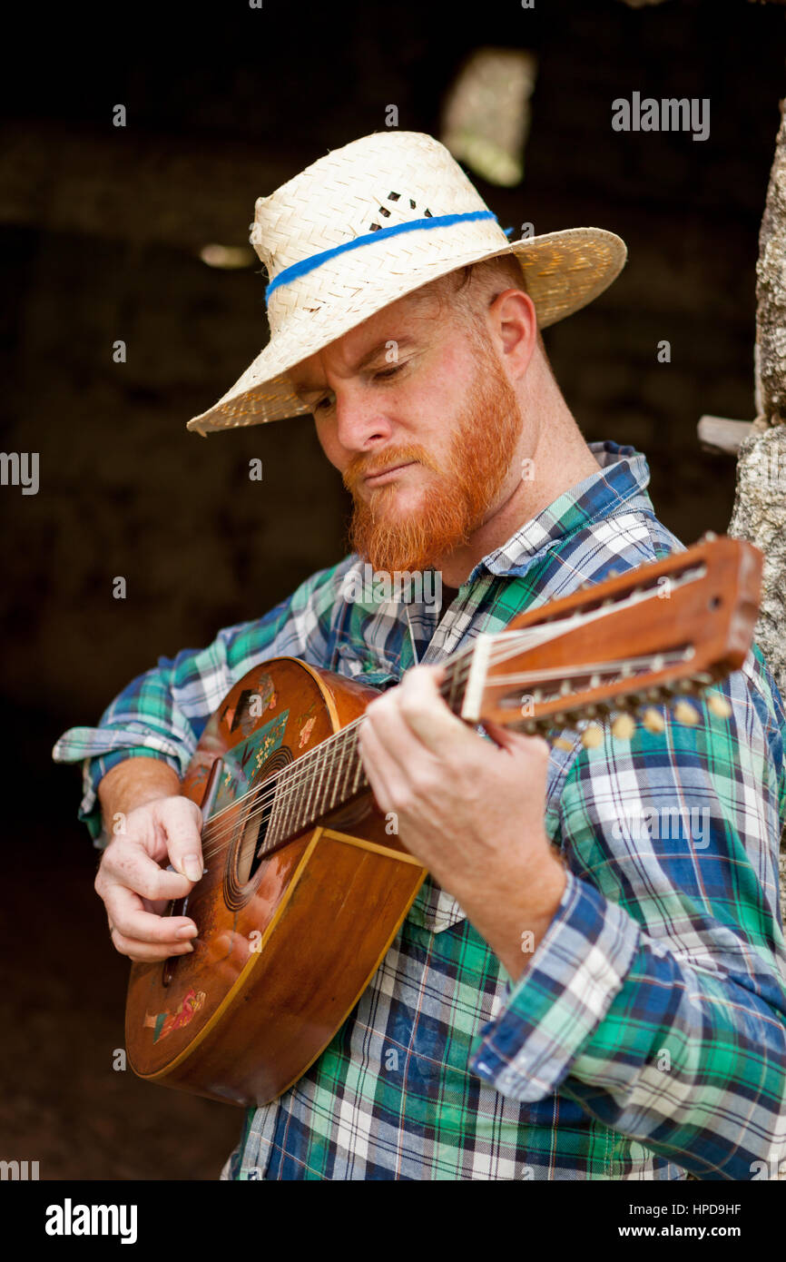Hipster man with red beard playing the guitar in a rural enviroment ...