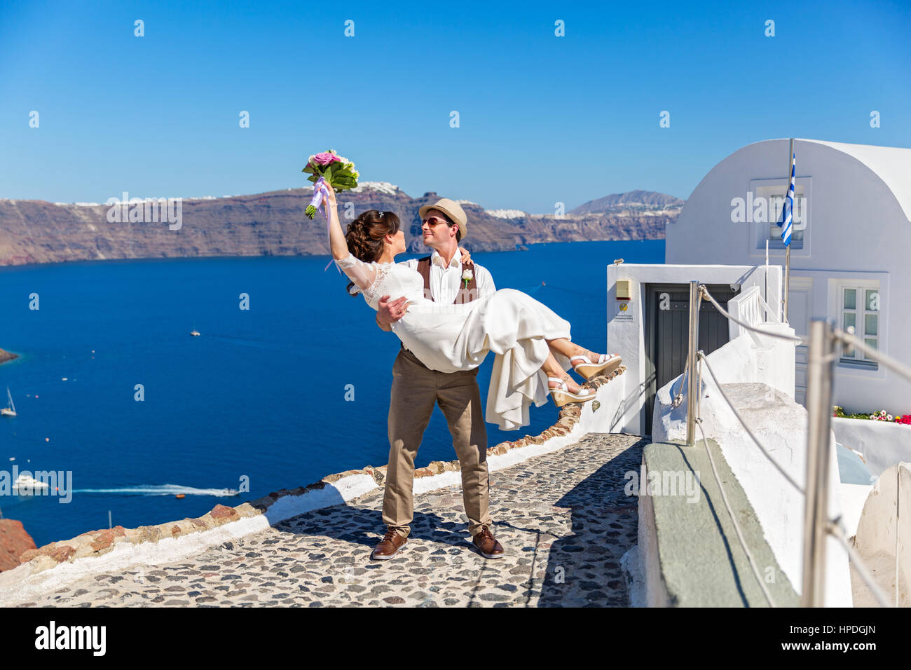 Cheerful wedding couple on Santorini island, Greece. Groom is holding ...