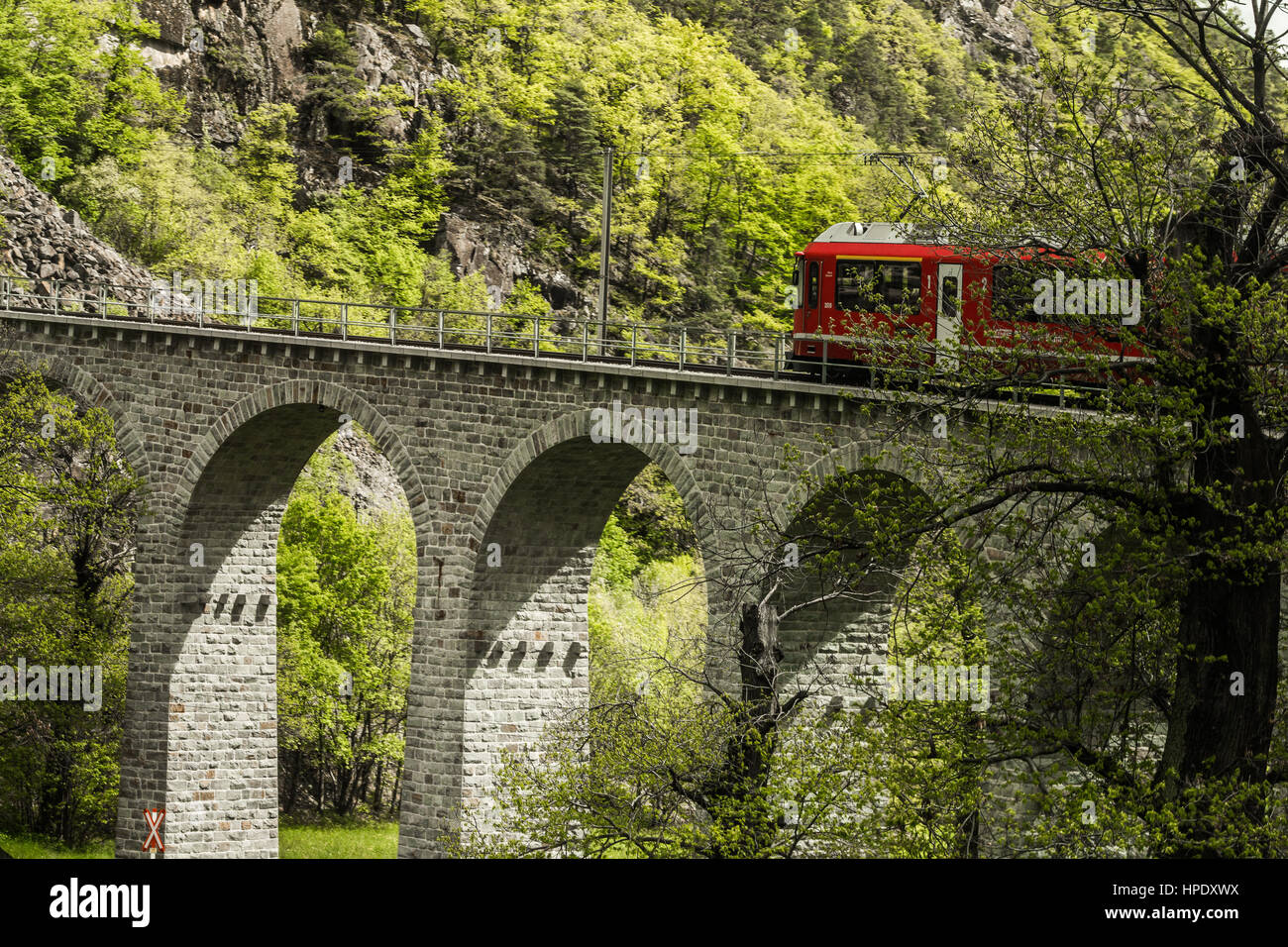 Red Train on Bridge crossing the green mountains and nature Stock Photo ...