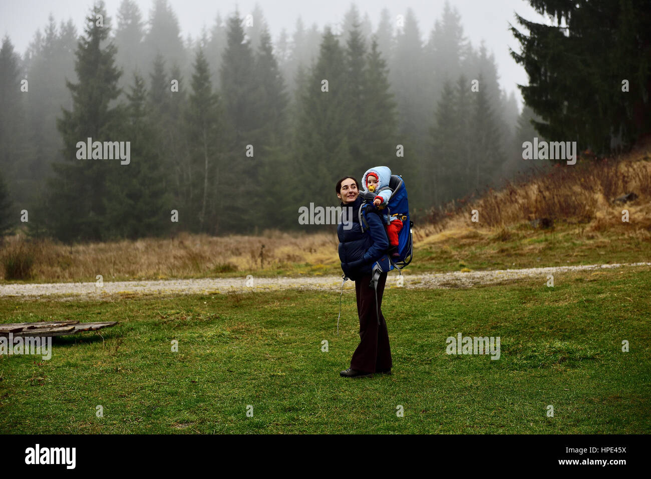 Young mother trekking, carrying her baby in a baby backpack child ...