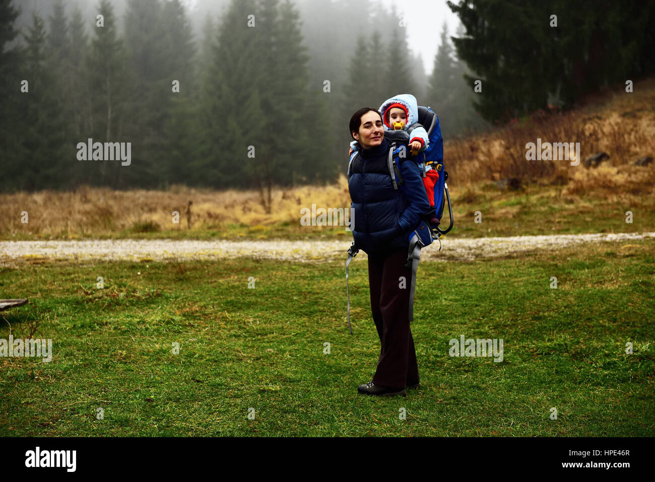 Young mother trekking, carrying her baby in a baby backpack child ...