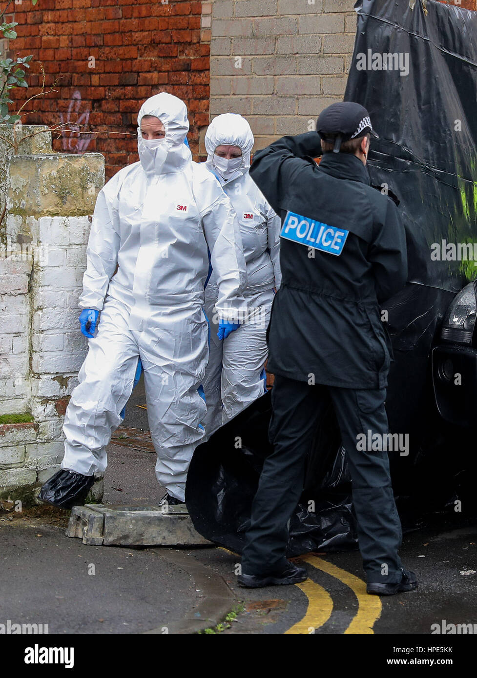 Forensic officers leave the scene through a fenced off alleyway on ...