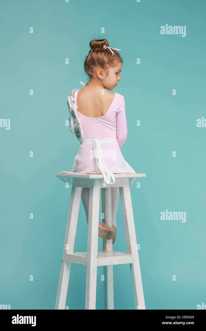 The back view of little girl as balerina dancer sitting on white wooden ...
