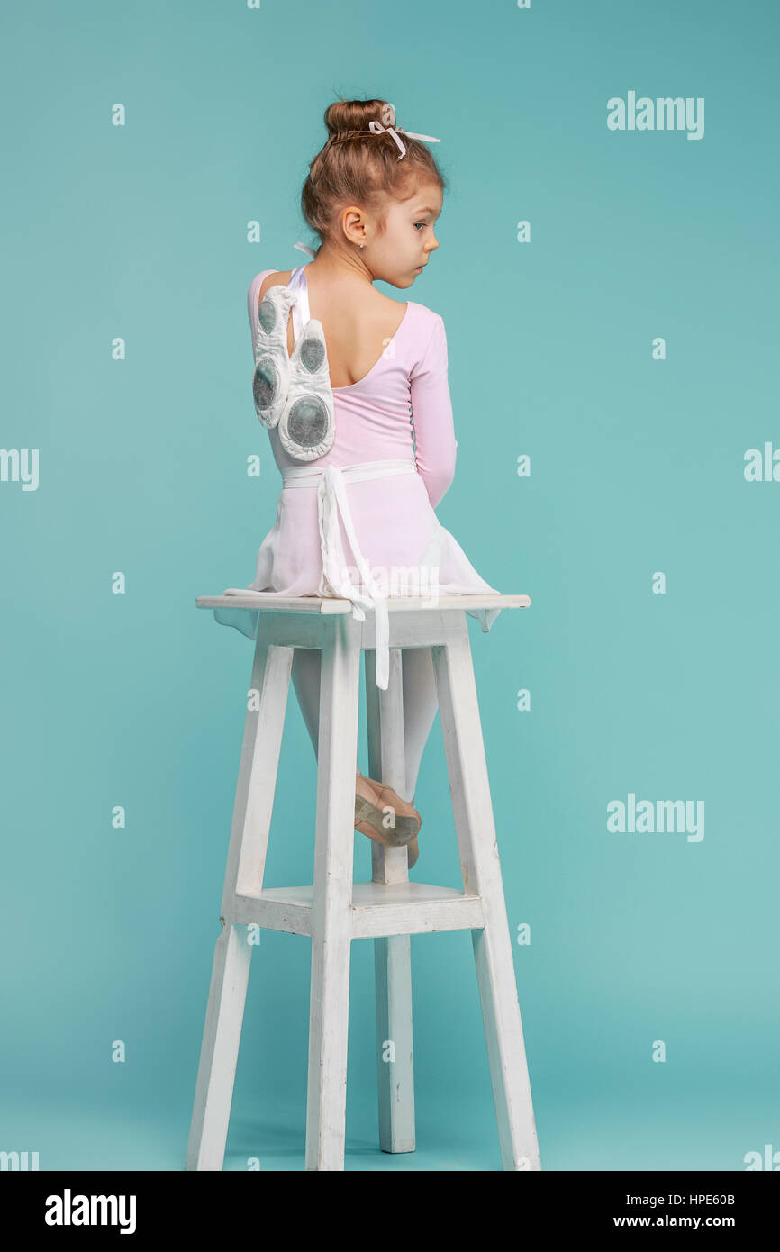The back view of little girl as balerina dancer sitting on white wooden ...