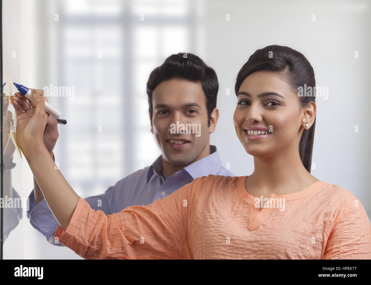 Two smiling colleagues in office writing on white board Stock Photo - Alamy