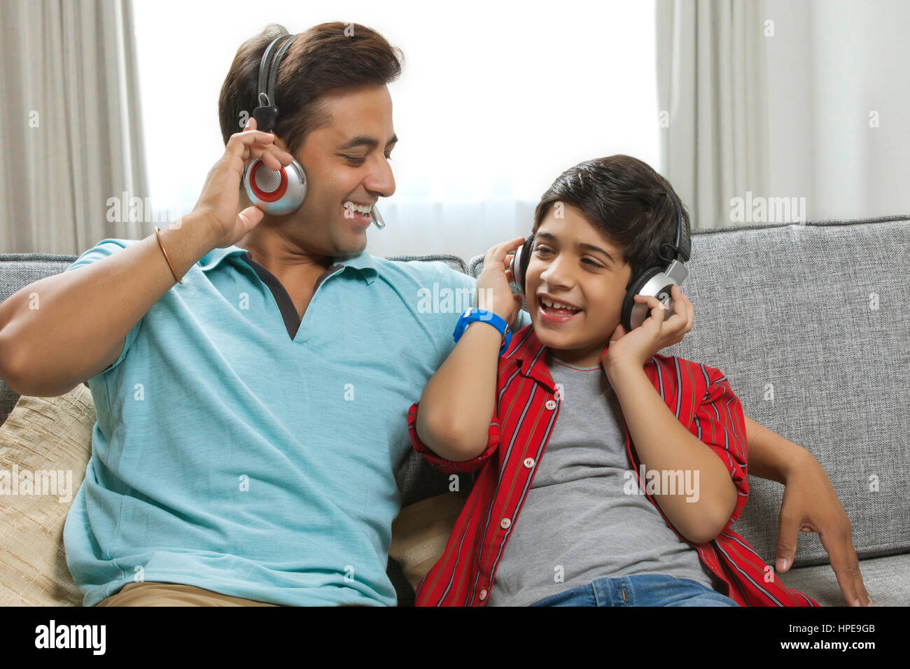 Father and son listening to music together on sofa with headphones ...