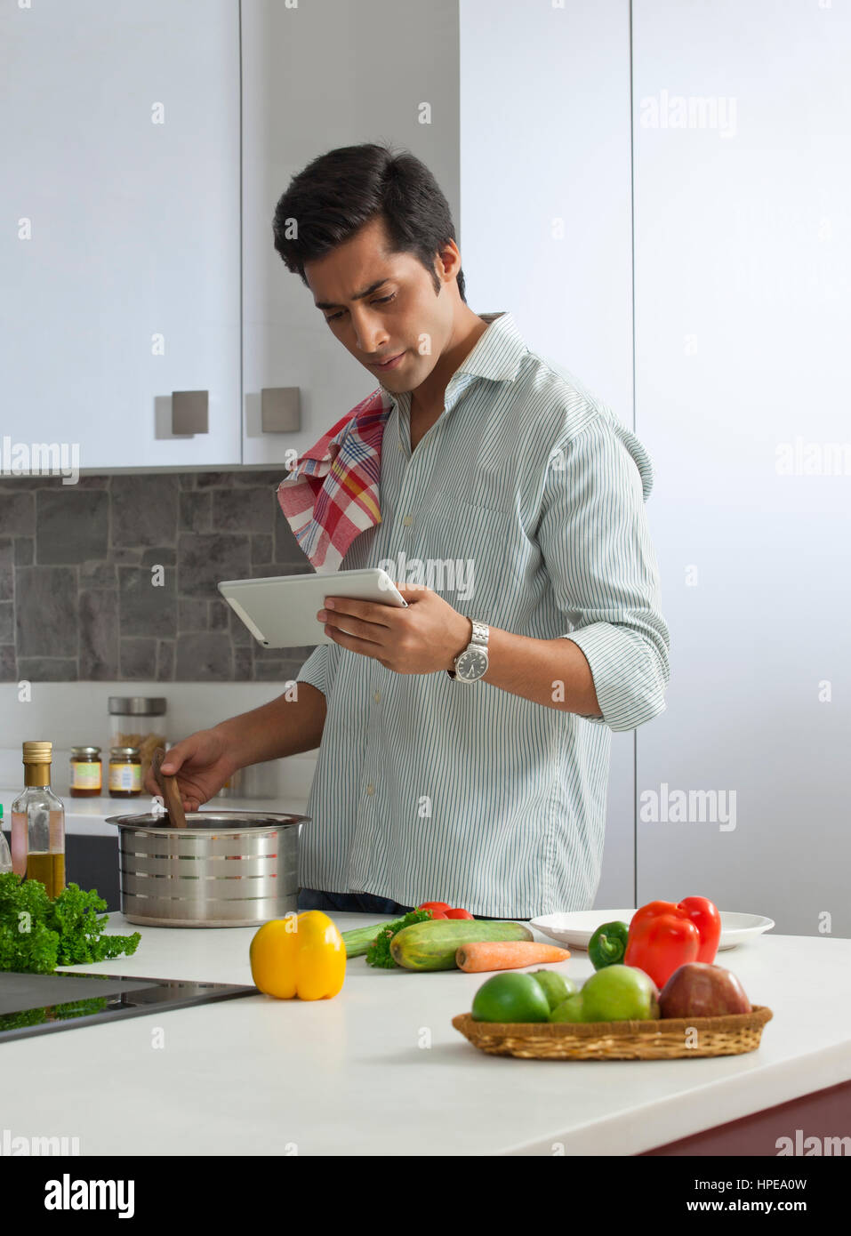 Man cooking in the kitchen while reading a recipe on digital tablet ...