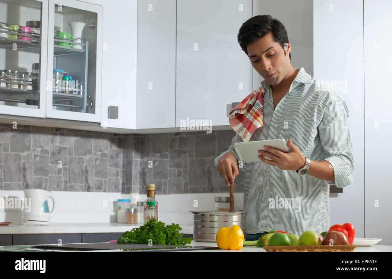 Man cooking in the kitchen while reading a recipe on digital tablet ...