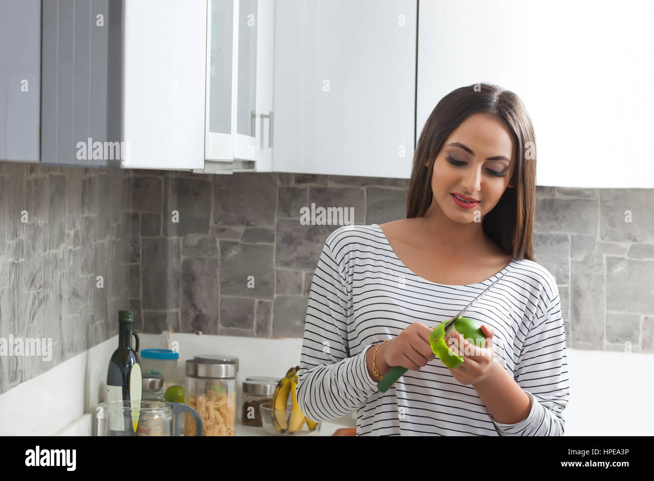 Young woman peeling orange in kitchen Stock Photo - Alamy