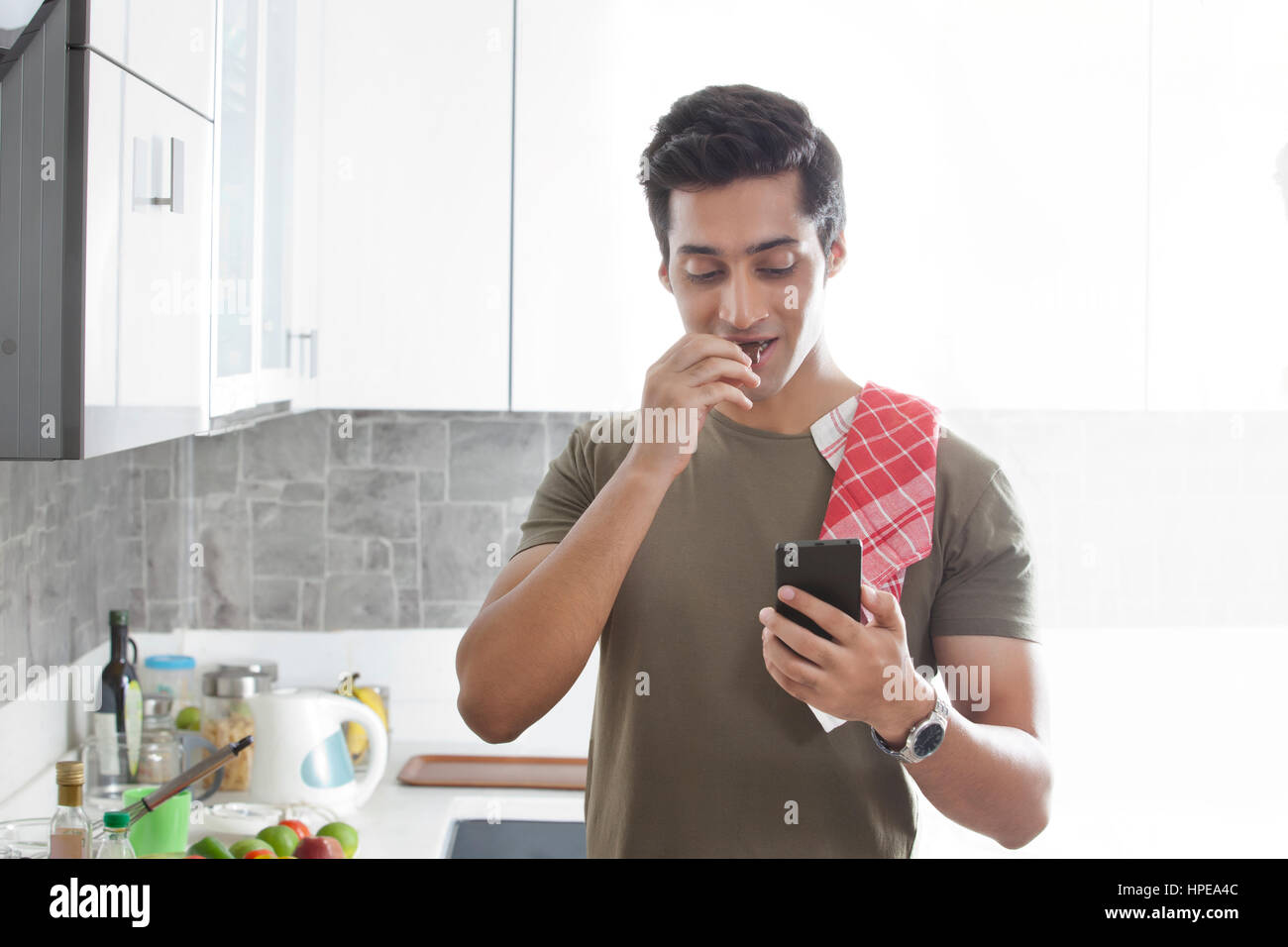 Young man using mobile phone and eating biscuit in kitchen Stock Photo ...