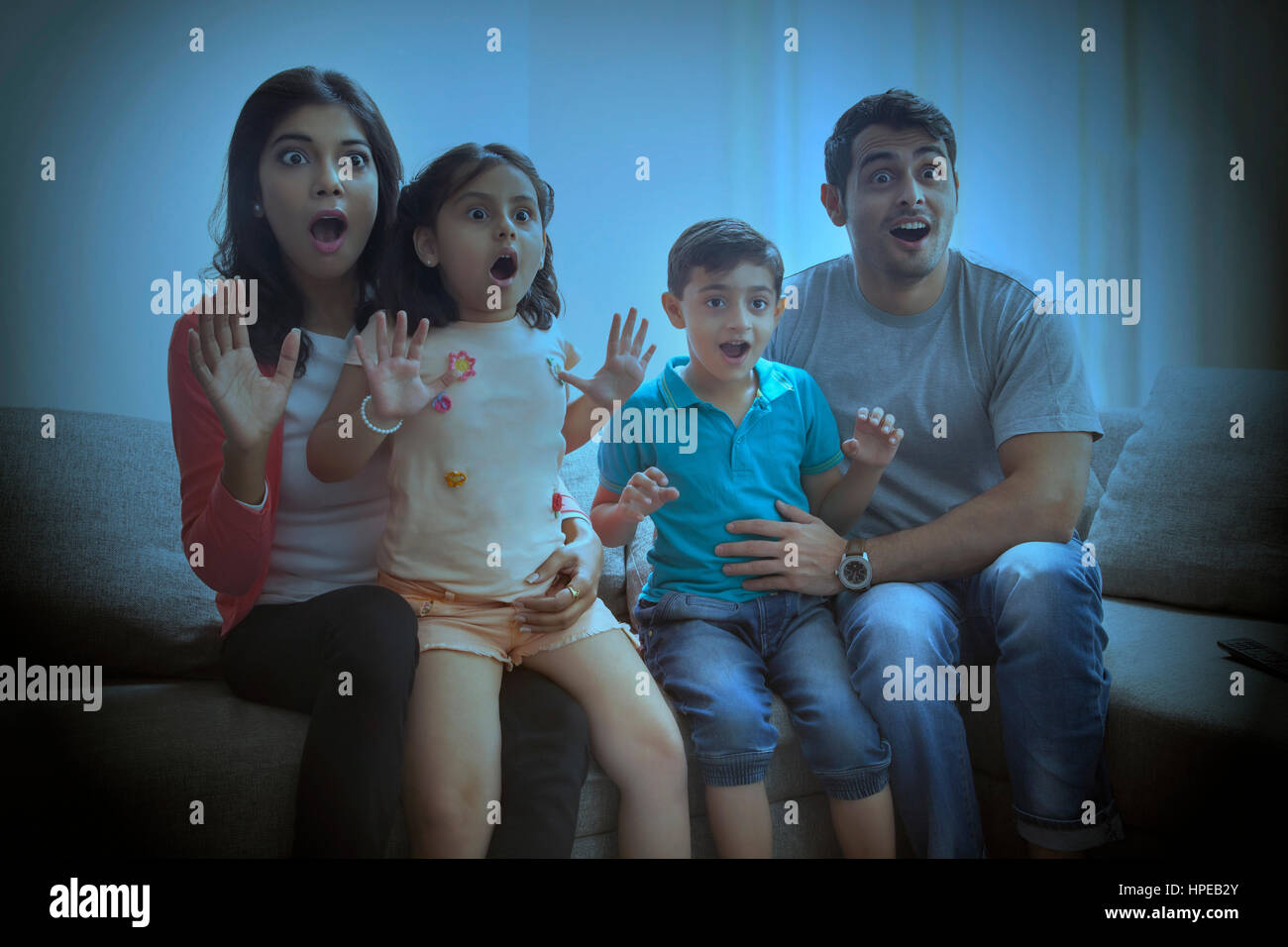 Family watching television together in living room looking shocked ...