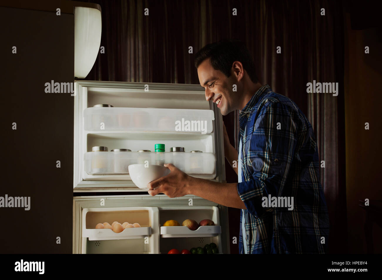 Young man standing in the kitchen searching food in the fridge at night ...