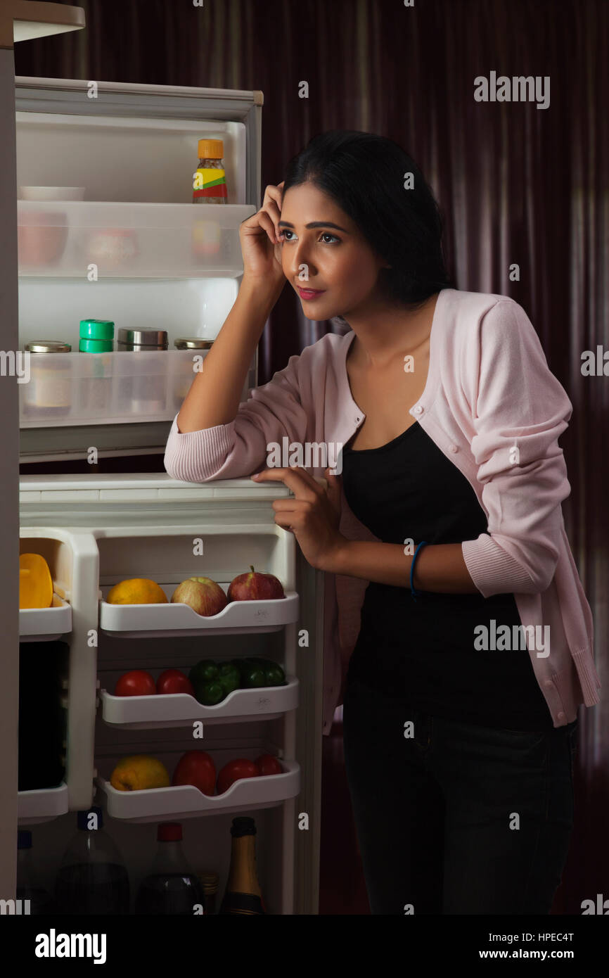 Young woman standing in front of open refrigerator and thinking Stock ...