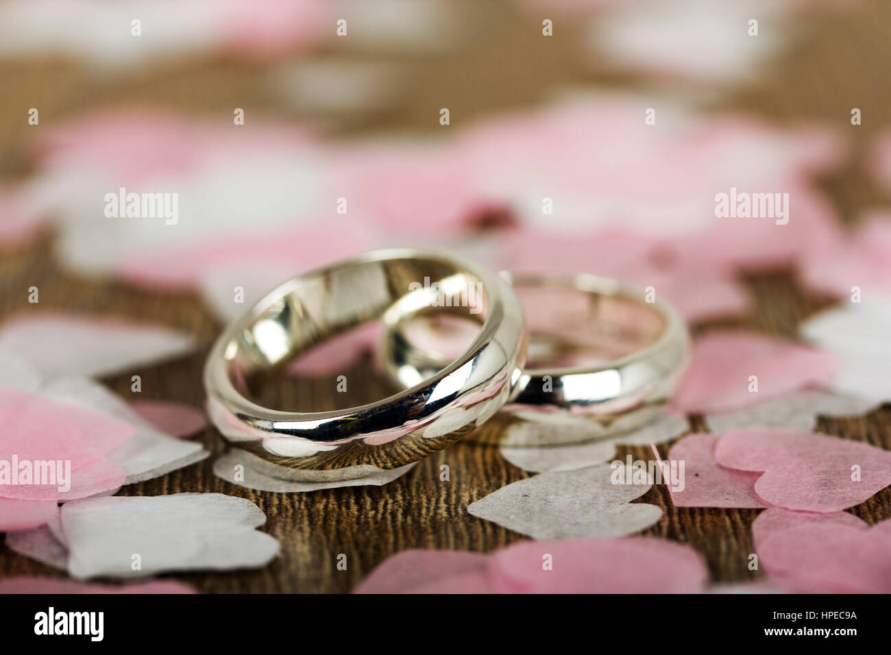pair of white gold wedding rings on a wooden background with confetti ...