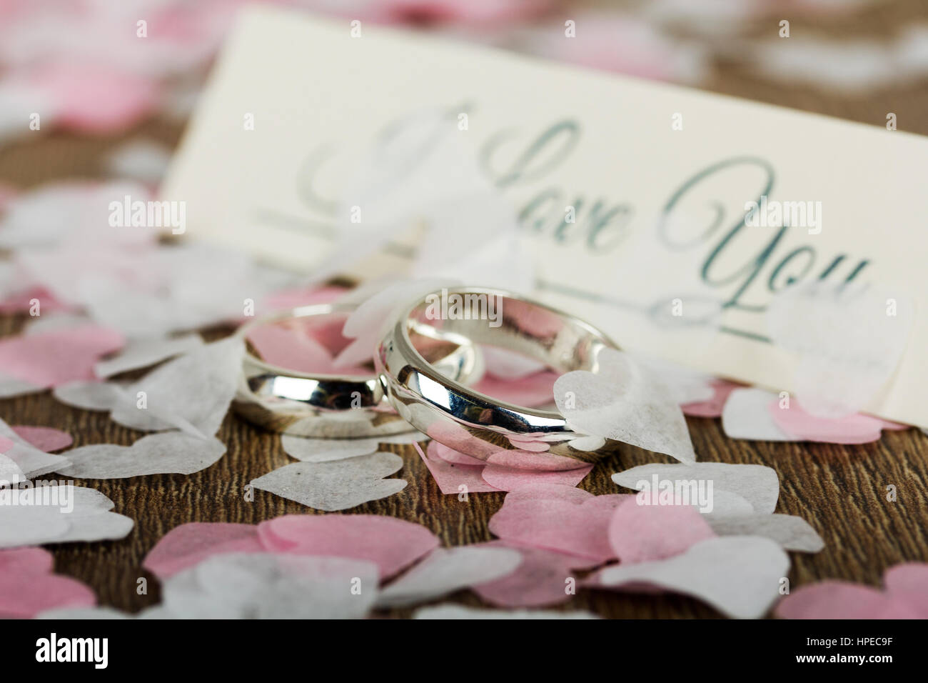 pair of white gold wedding rings on a wooden background with confetti ...