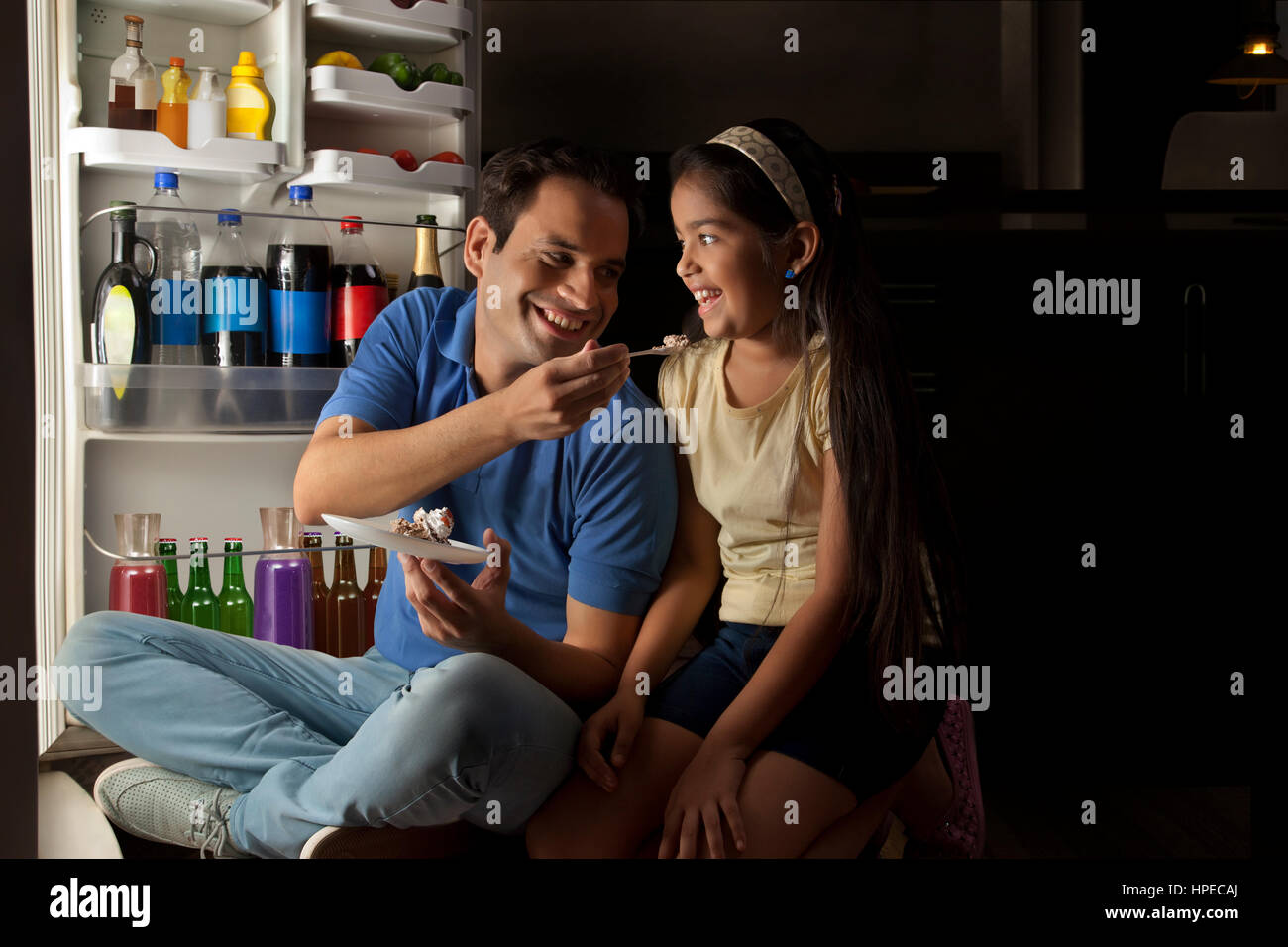 Father feeding cake to daughter in front of open refrigerator Stock ...