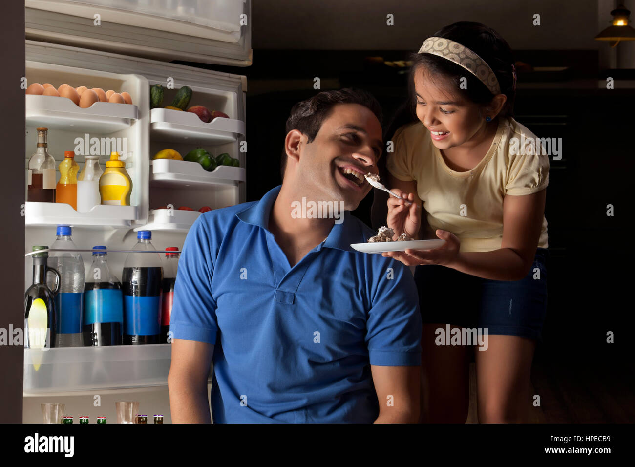 Daughter feeding cake to father in front of open refrigerator Stock ...
