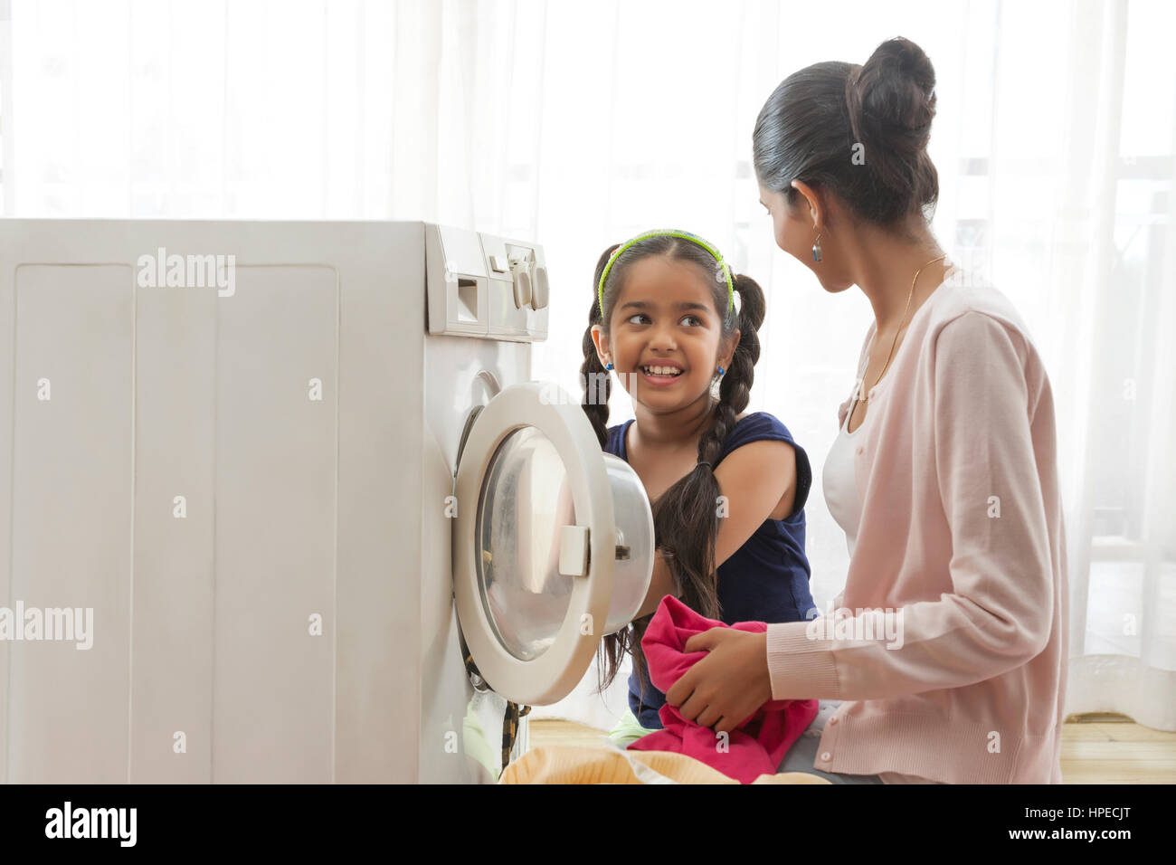 Smiling mother and daughter loading washing machine Stock Photo - Alamy