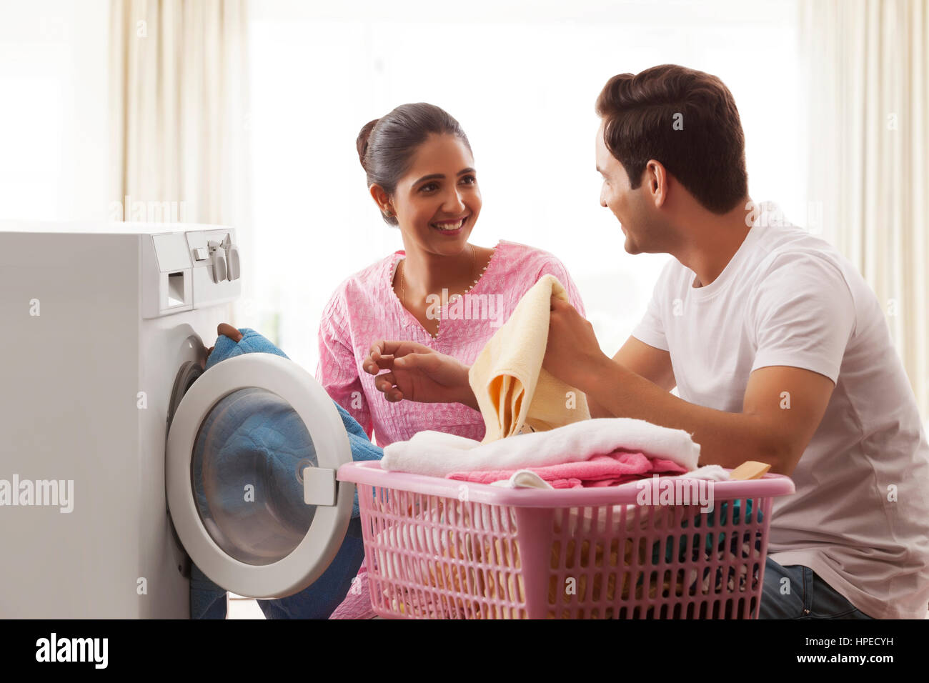 Smiling young couple loading washing machine together Stock Photo - Alamy