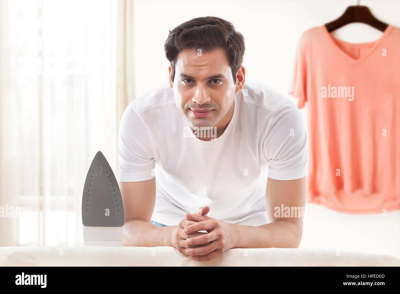 Portrait young man with ironing board and top hanging on wall at home ...